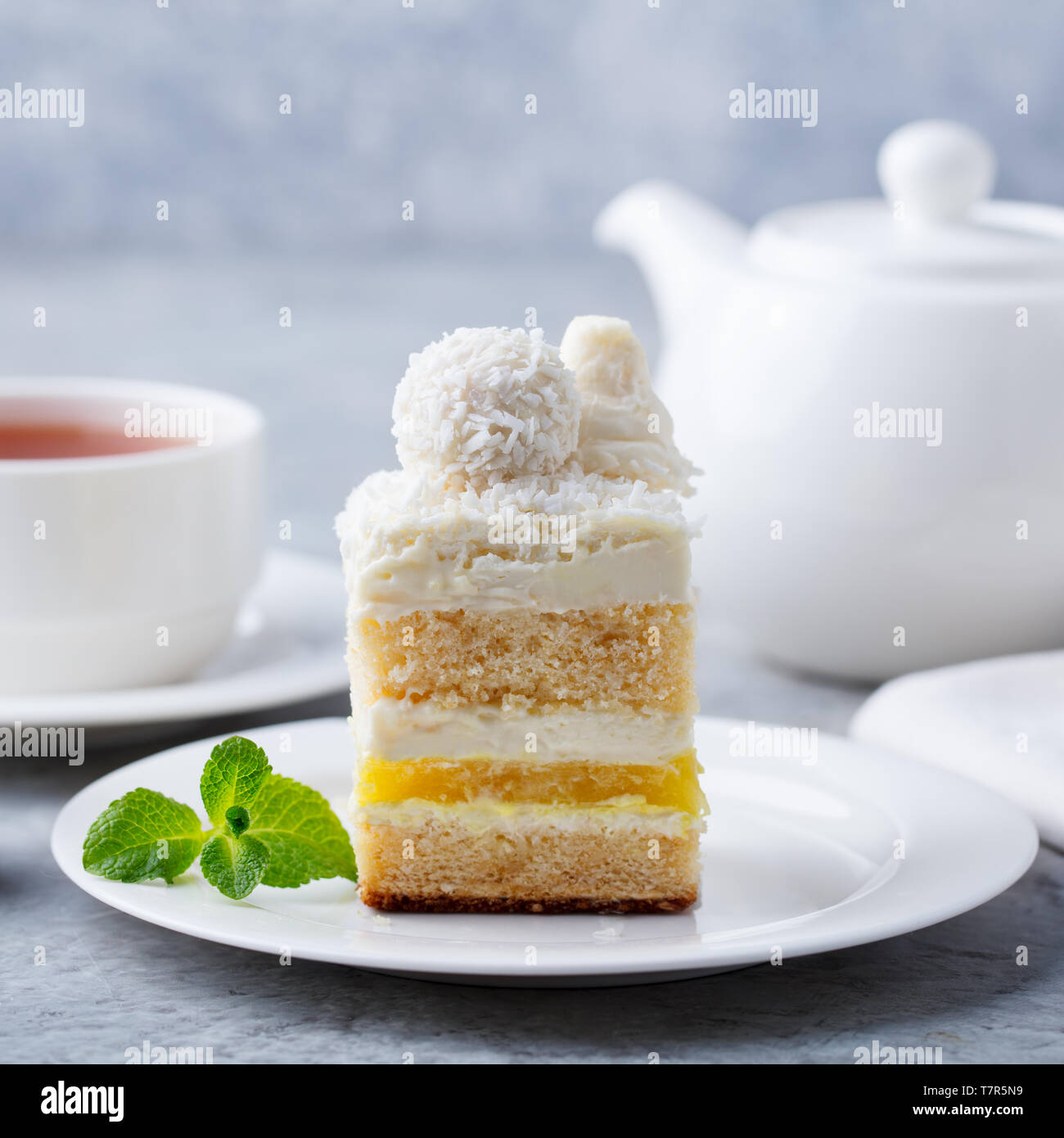 Coconut layered, raffaello cake on white plate. Grey background. Close ...