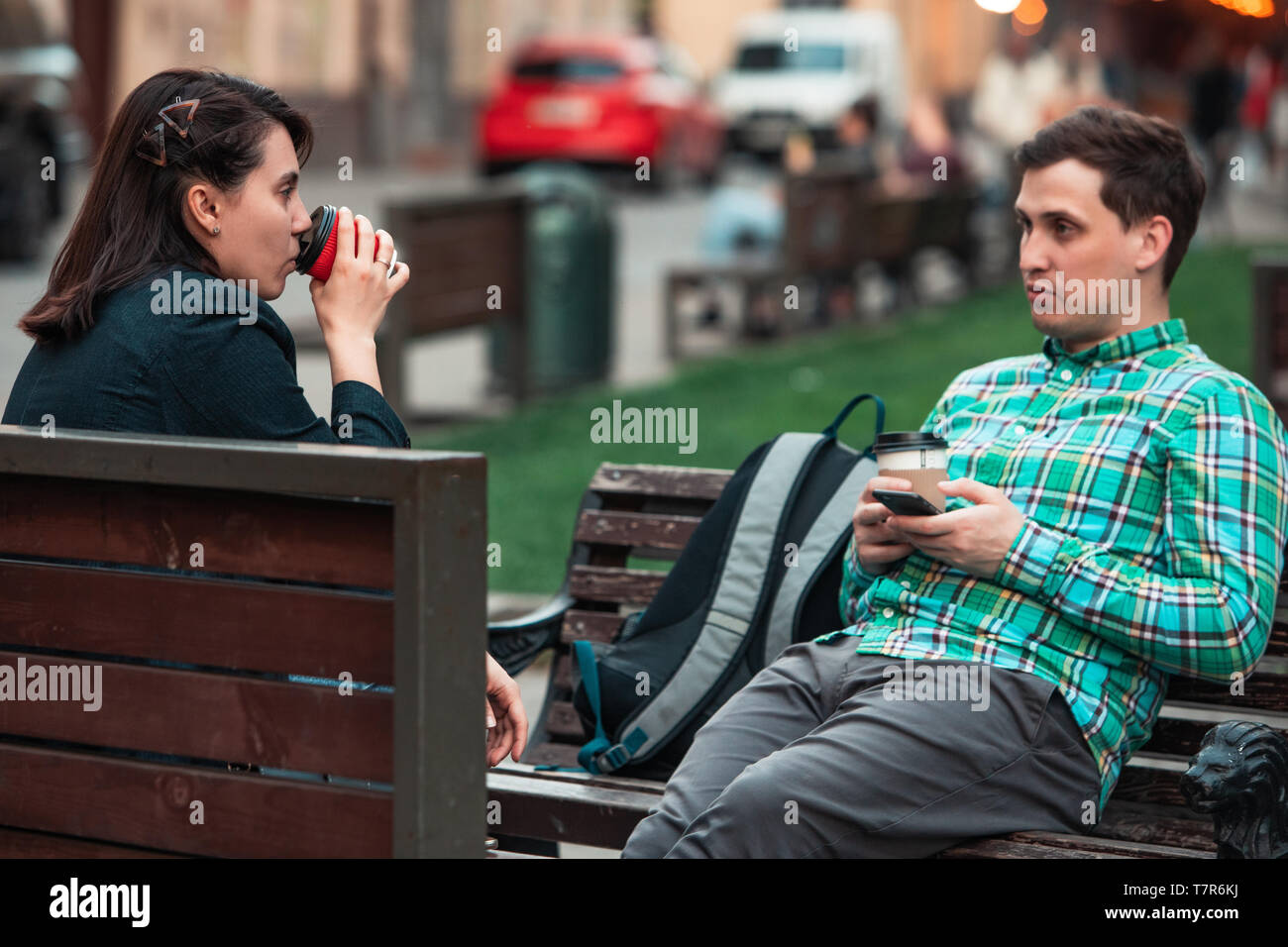 smiling couple sitting on bench talking to each other drinking coffee ...