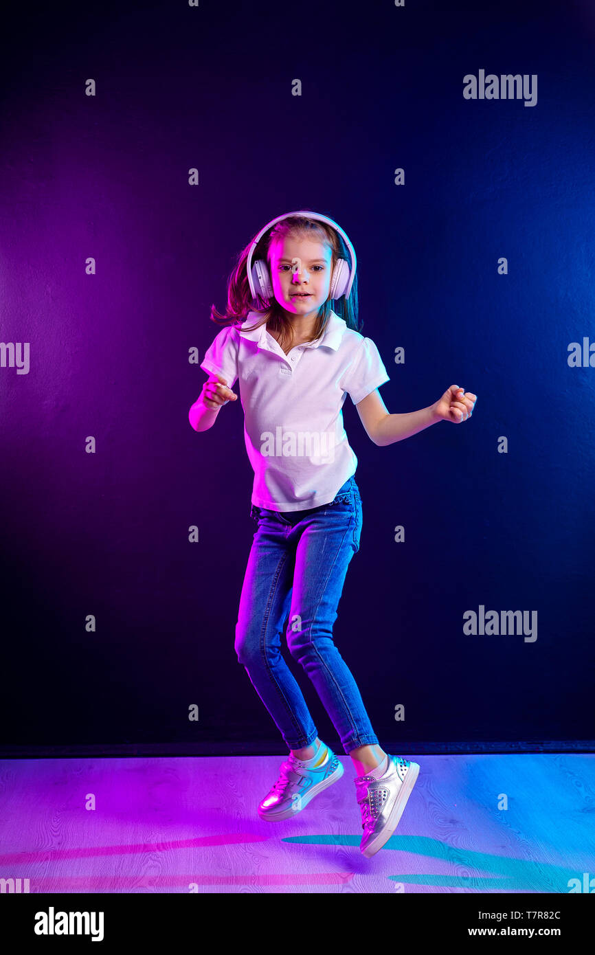 Girl of 7 years old listening to music in headphones and jump on dark ...
