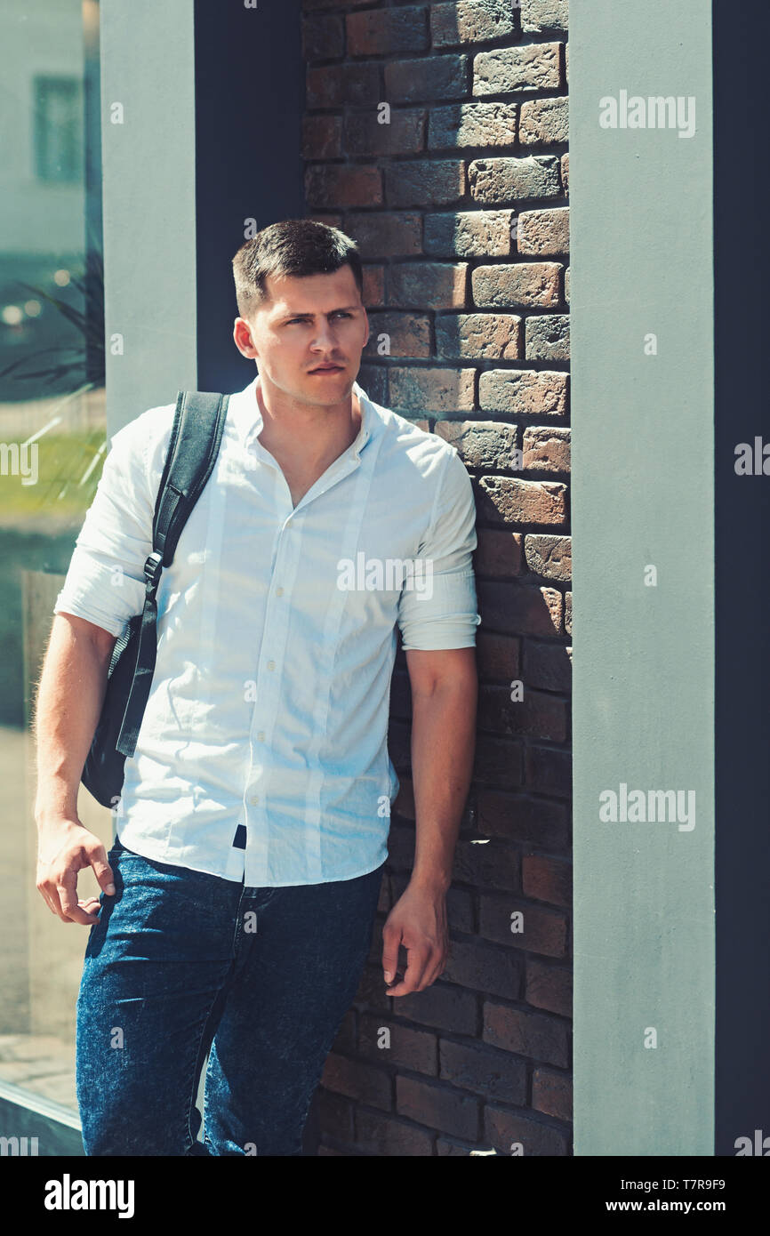 Handsome young man carrying backpack near walls of building Stock Photo ...