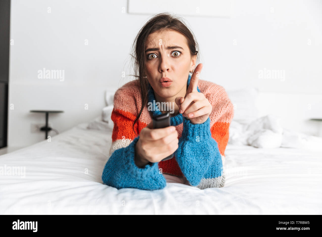 Portrait of cheerful woman 20s holding remote control while lying in ...