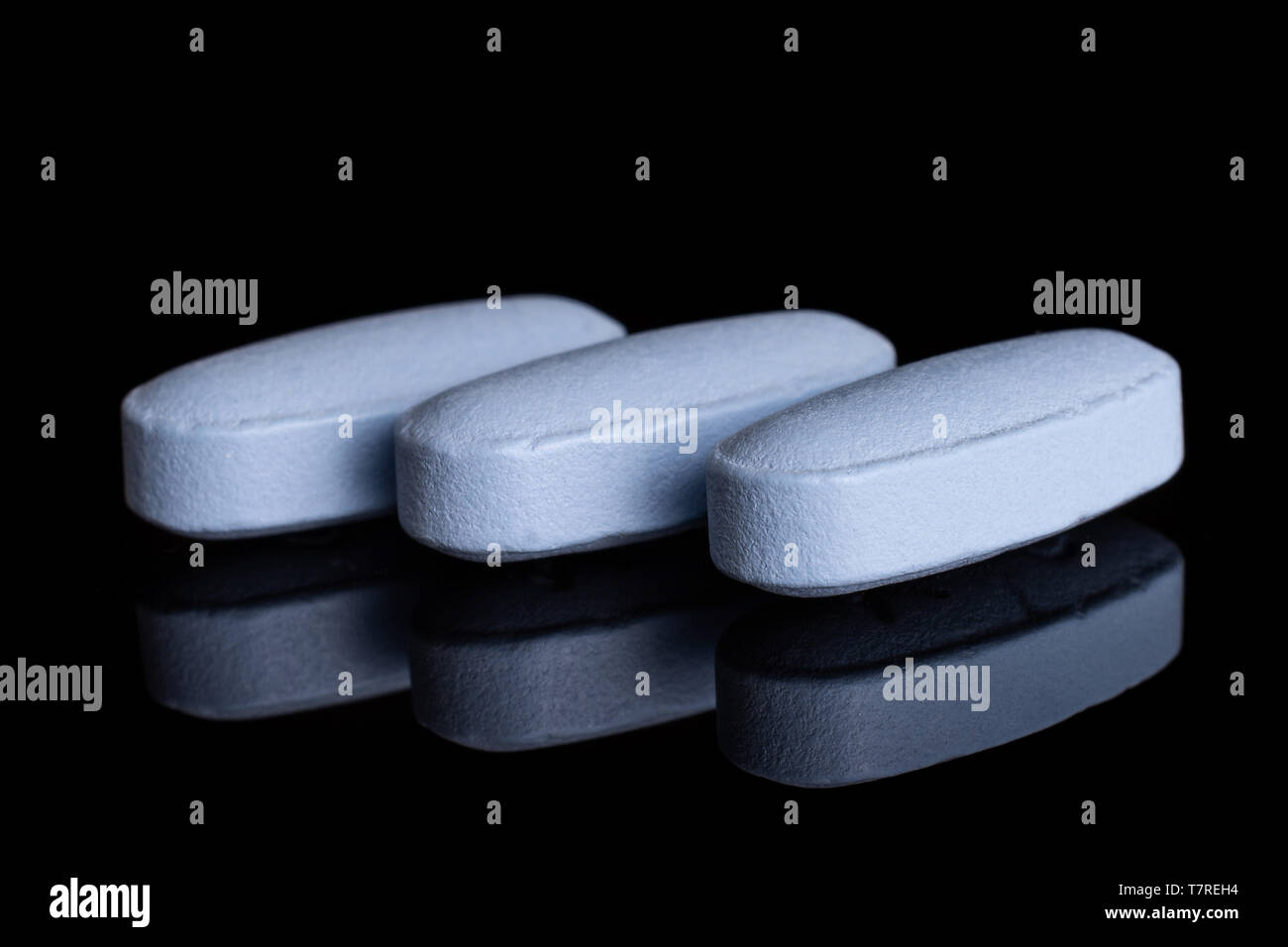 Closeup of three whole blue medical drug isolated on black glass Stock ...