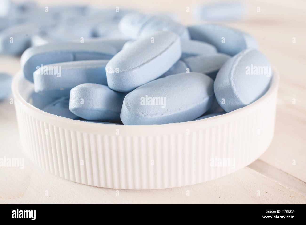 Closeup of lot of whole blue medical drug in a white cap on white wood ...