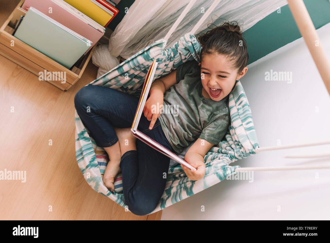 little girl laughs out loud reading a book at home near the window ...