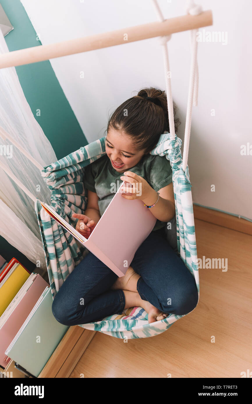 little girl laughs out loud reading a book at home near the window ...