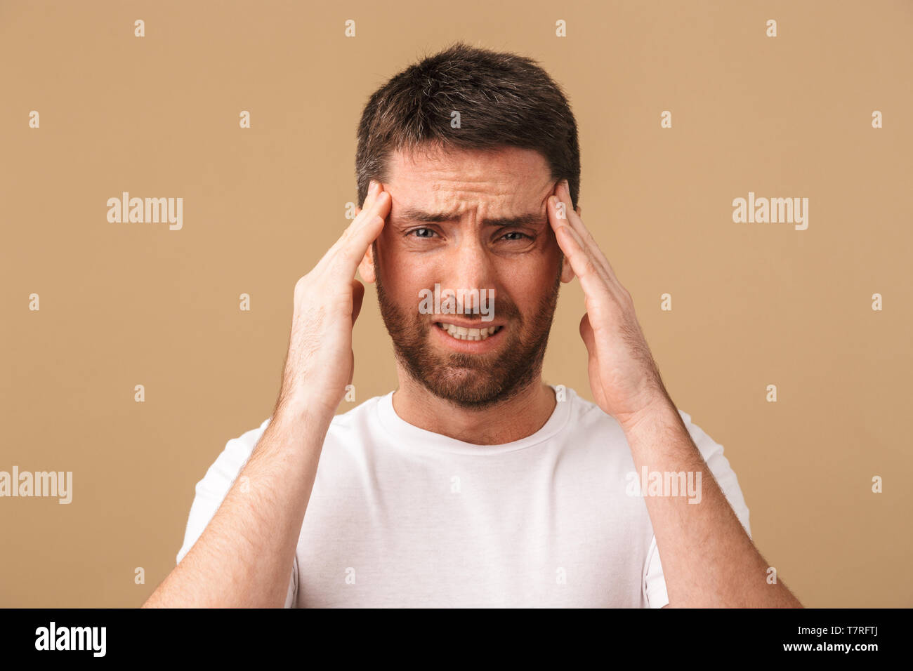 Portrait of a tired young man suffering from a headache isolated over ...