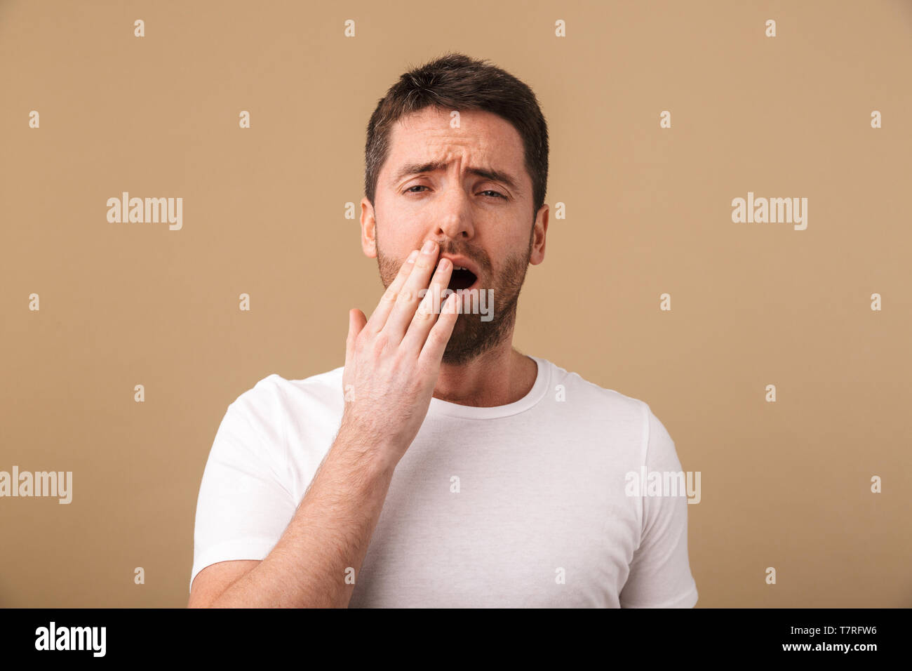 Portrait of a tired young man standing isolated over beige background ...