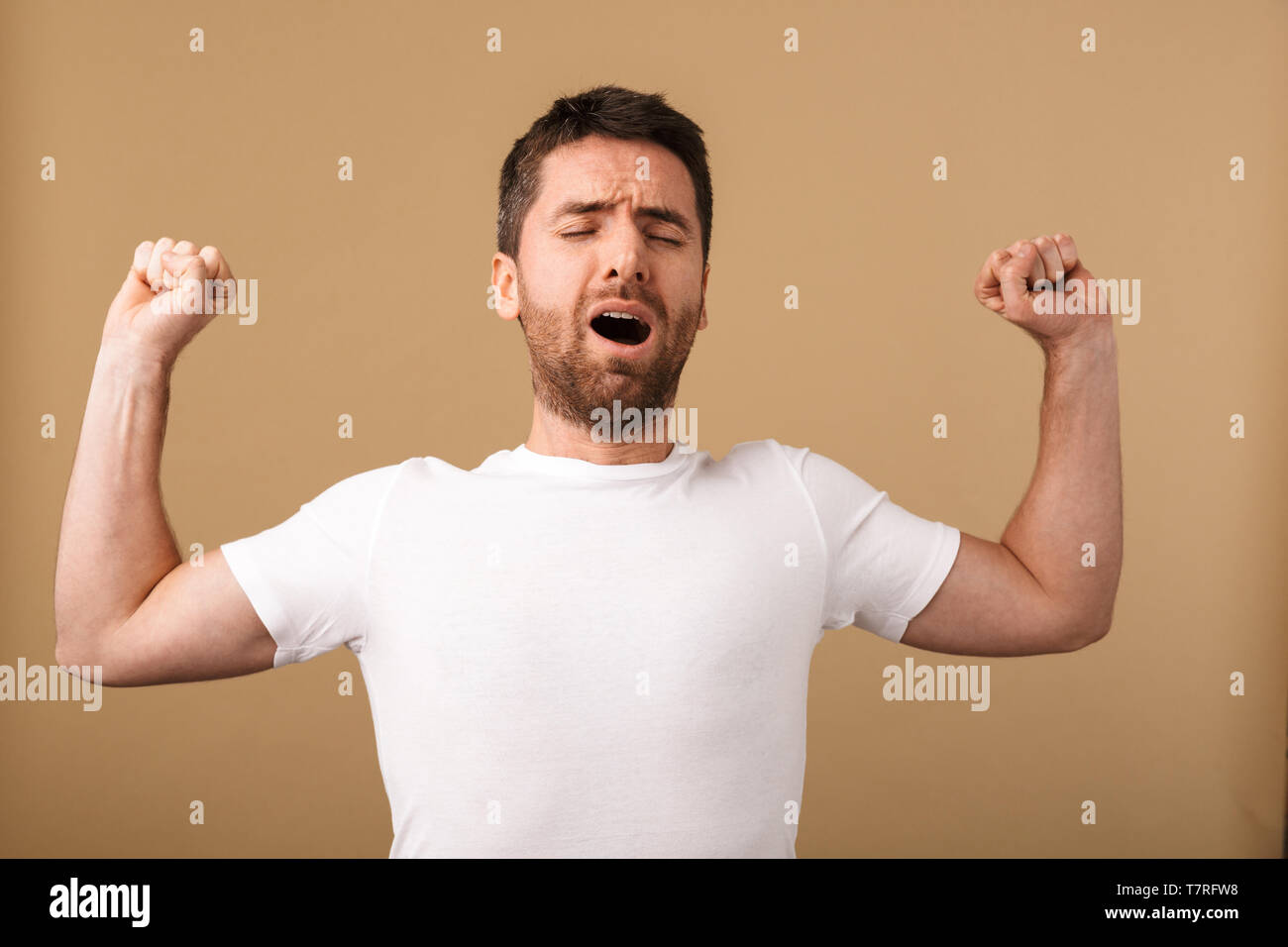Portrait of a tired young man standing isolated over beige background ...