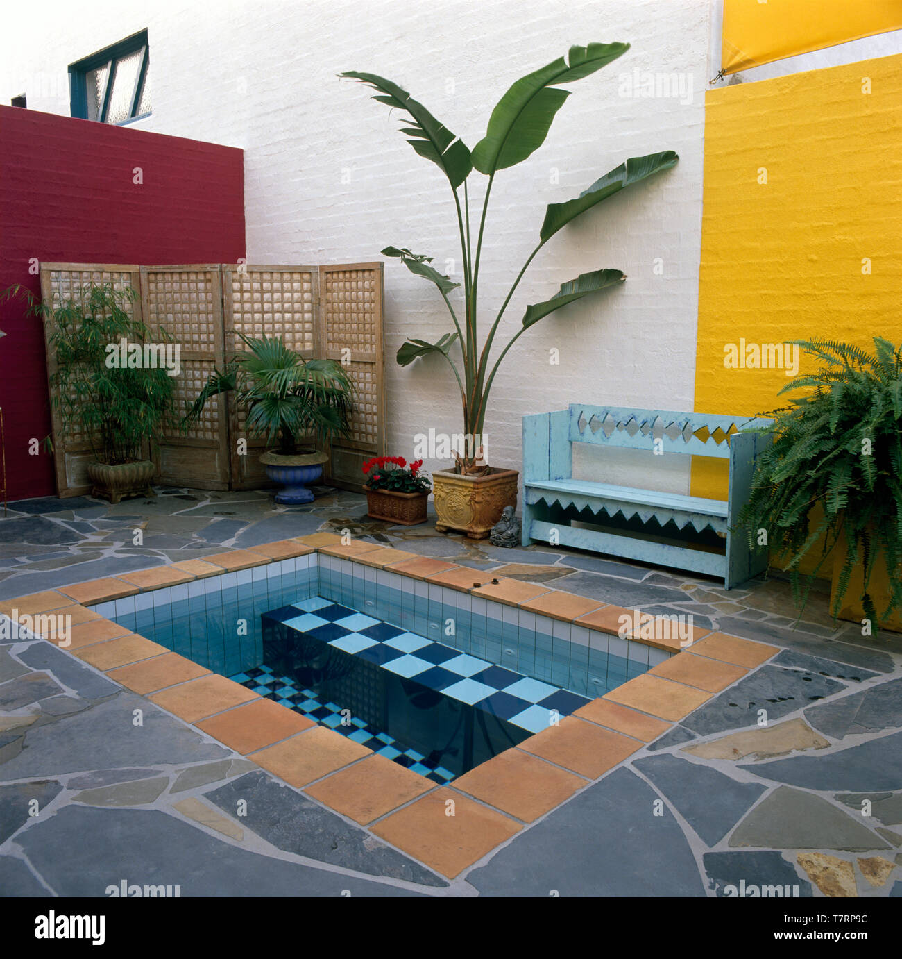 Tiled rectangular jacuzzi on patio with lush green plants in pots and a ...