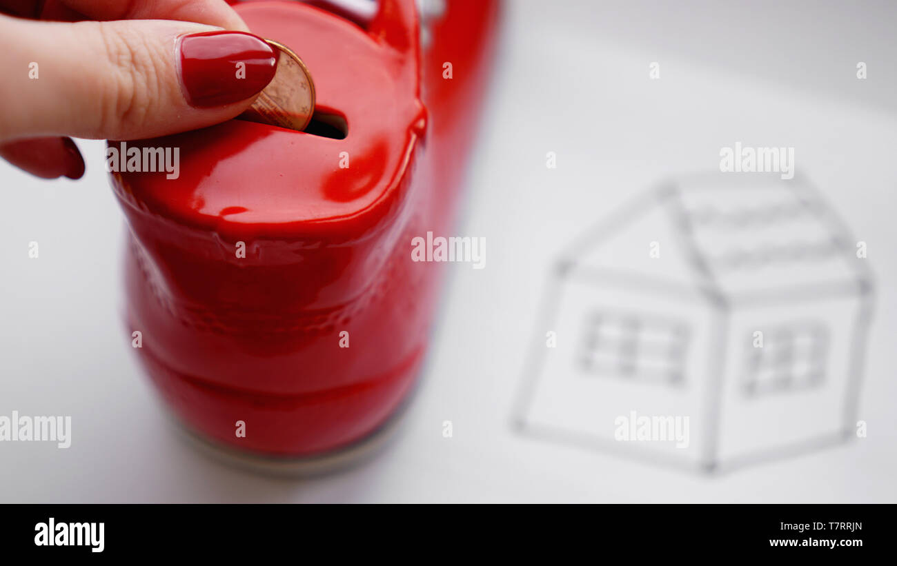 Hand dropping coin into the moneybox. Drawing a house on a white sheet ...