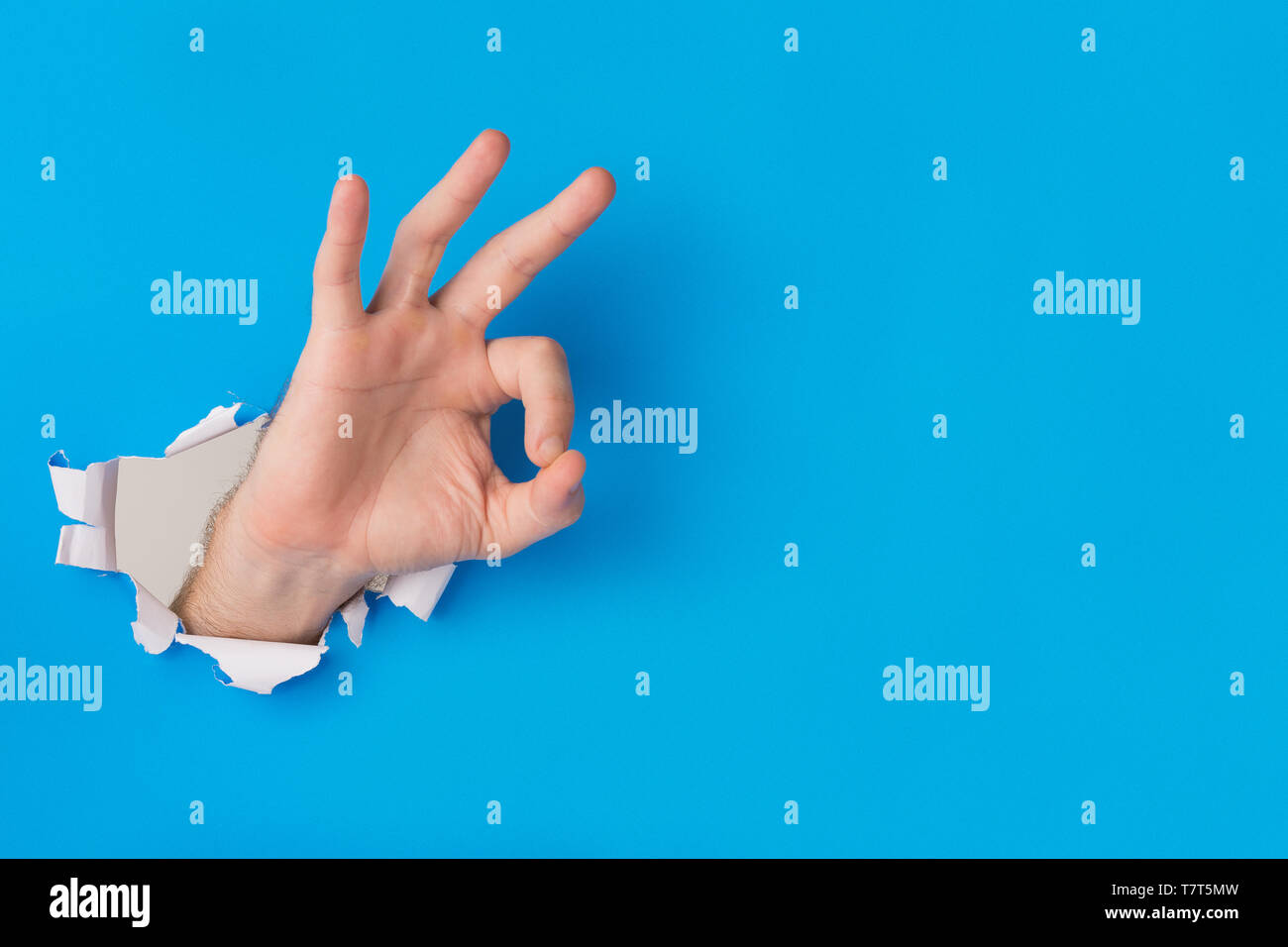 Male hand tearing through blue paper background creating ok gesture ...