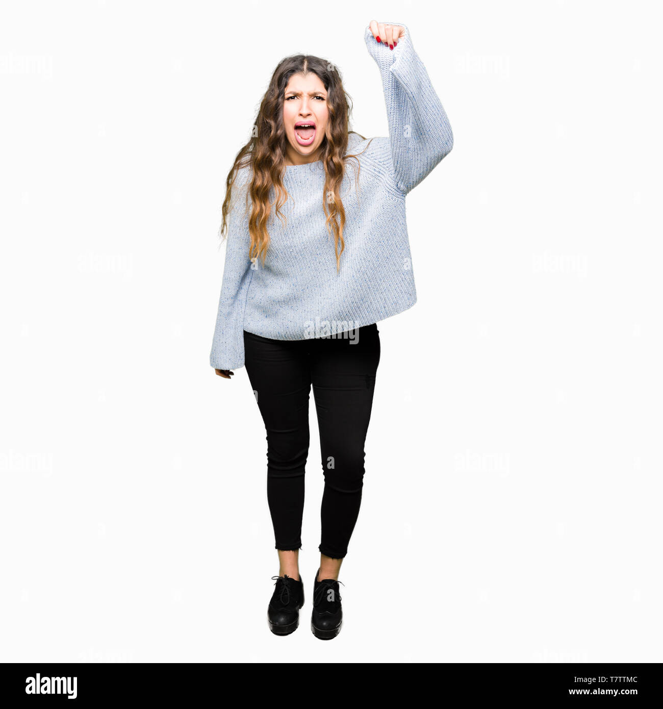 Young beautiful woman wearing winter sweater angry and mad raising fist ...