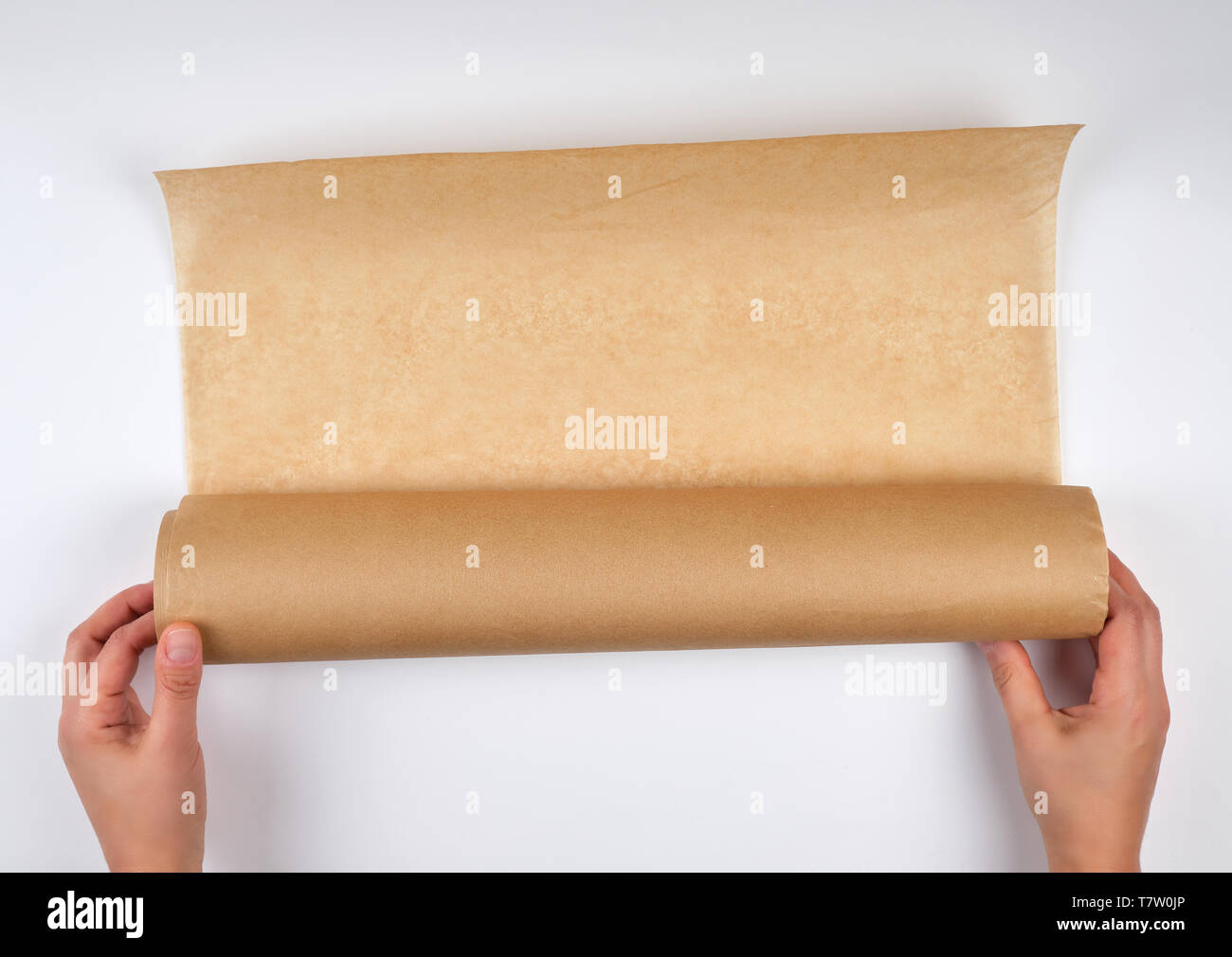two hands hold a large roll of brown parchment paper on a white ...