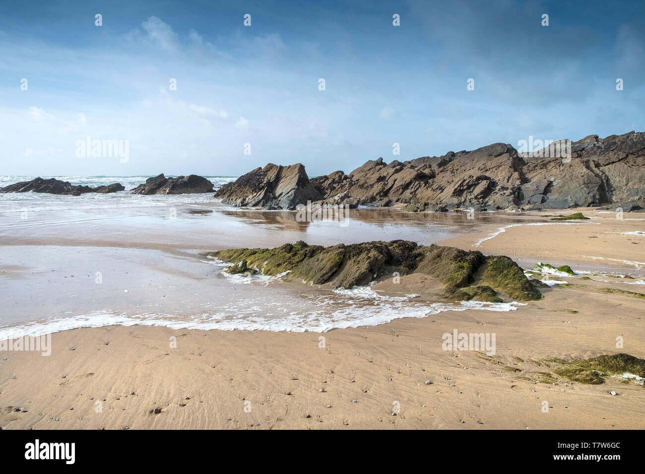 Incoming tide around rocks exposed by the low tide on Fistral Beach in ...