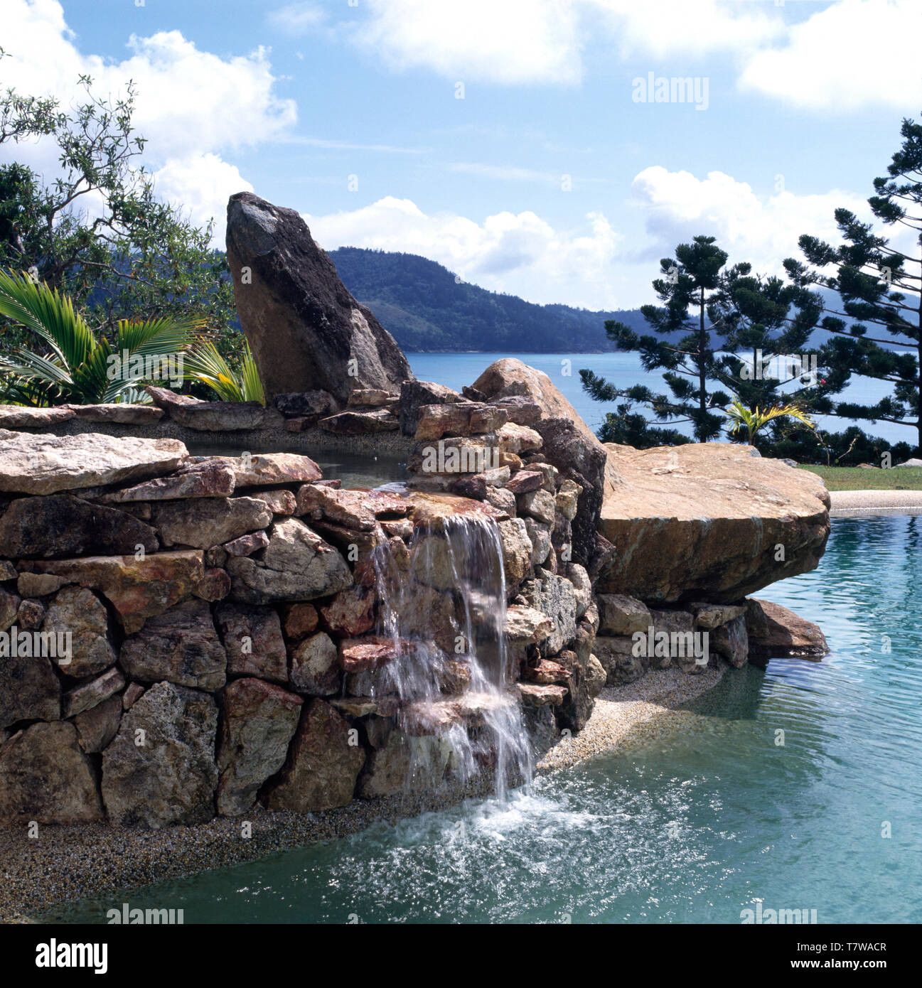 Small waterfall tumbling over rocks in a swimming pool beside the ocean ...