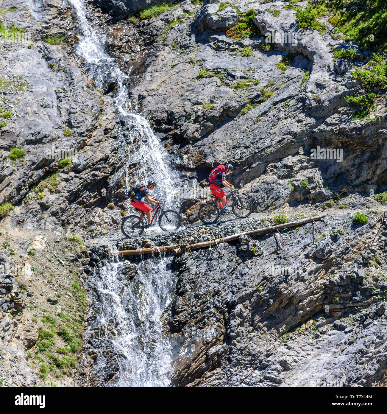 Two cyclists crossing a small waterfall at a steep rock wall on single ...