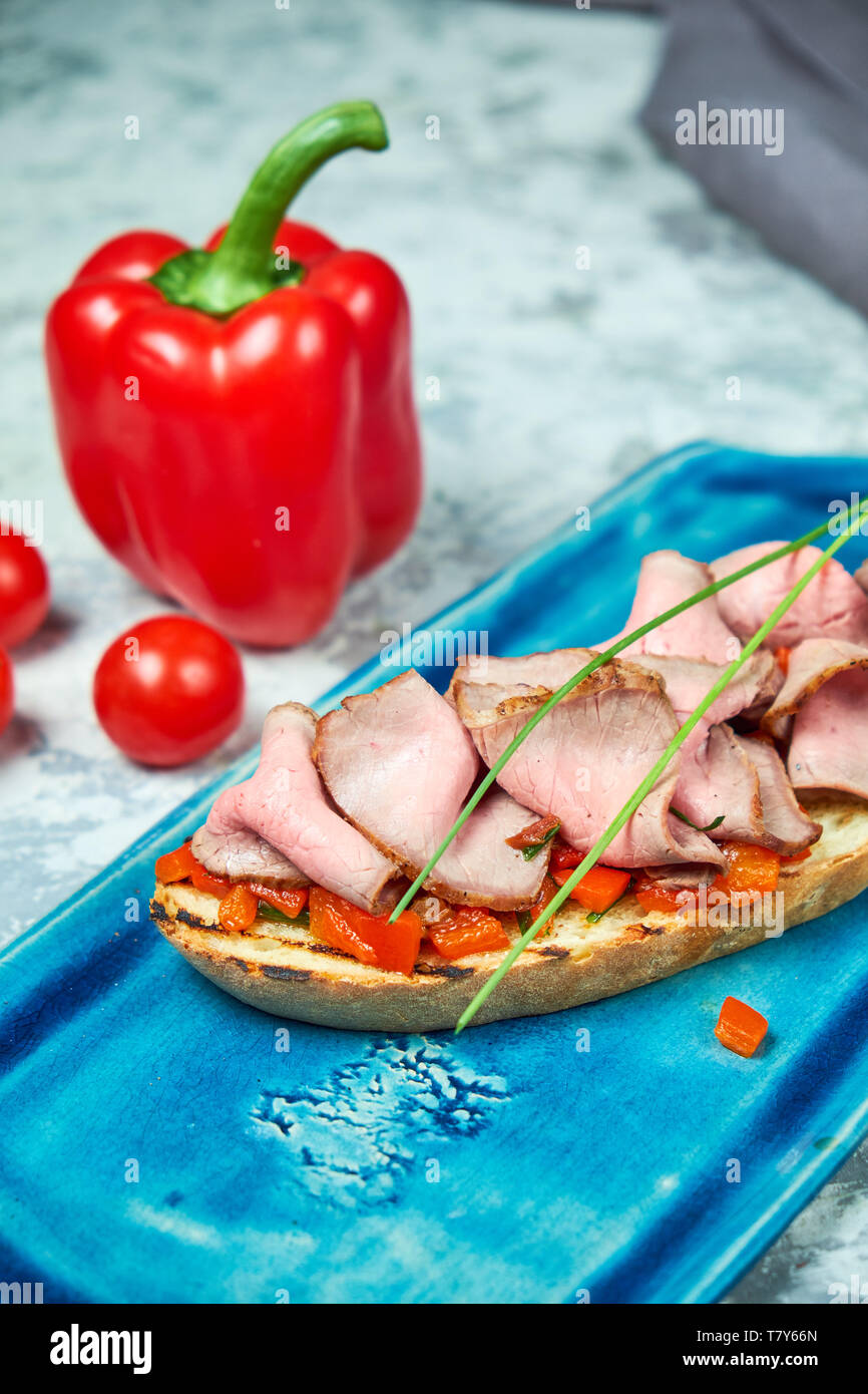 On a blue plate of bruschet with beef and tomatoes, next to it is a red ...