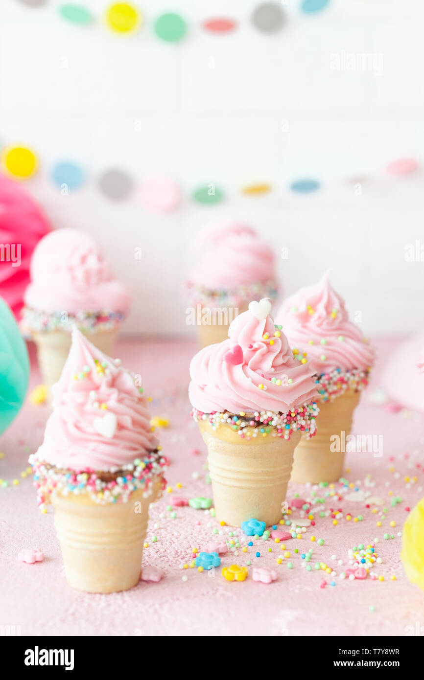 Pink soft serve ice cream with colorful sprinkles in little waffle cups ...