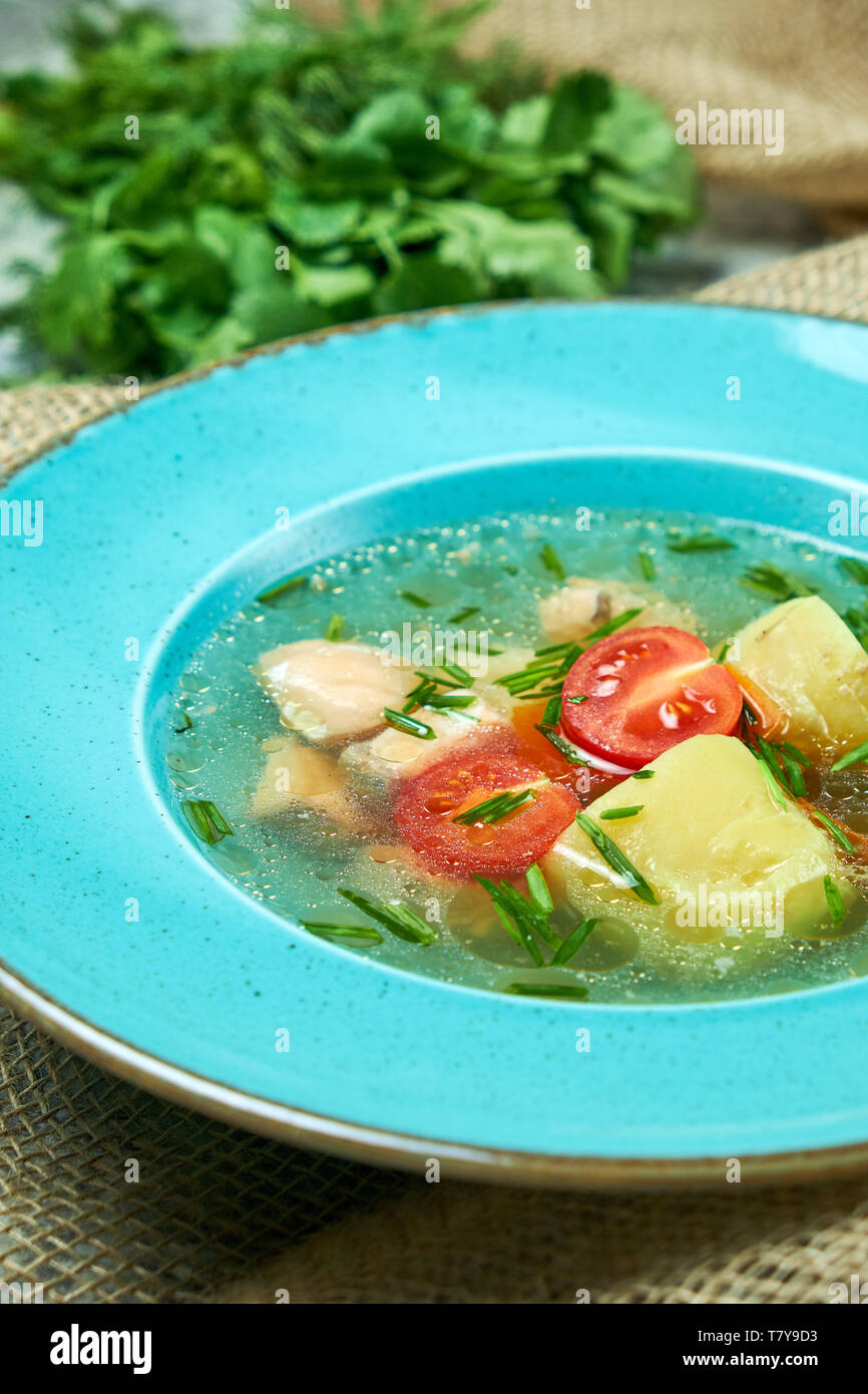 Red fish soup in a blue plate and a bunch of greens on a beige textured ...