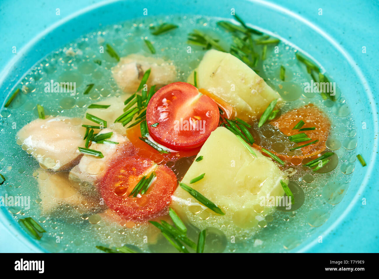 Red fish soup in a blue plate and a bunch of greens on a beige textured ...
