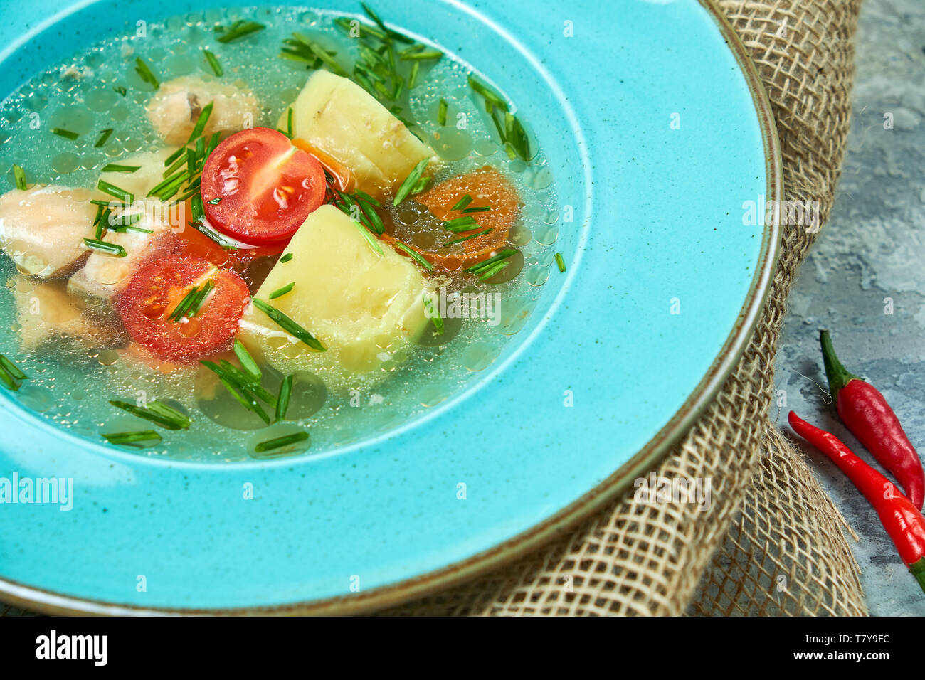 Red fish soup in a blue plate and a bunch of greens on a beige textured ...