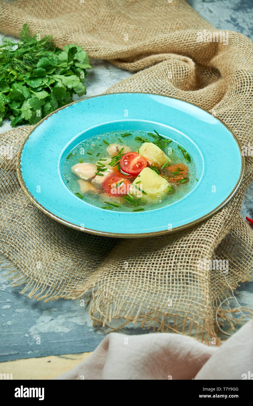 Red fish soup in a blue plate and a bunch of greens on a beige textured ...