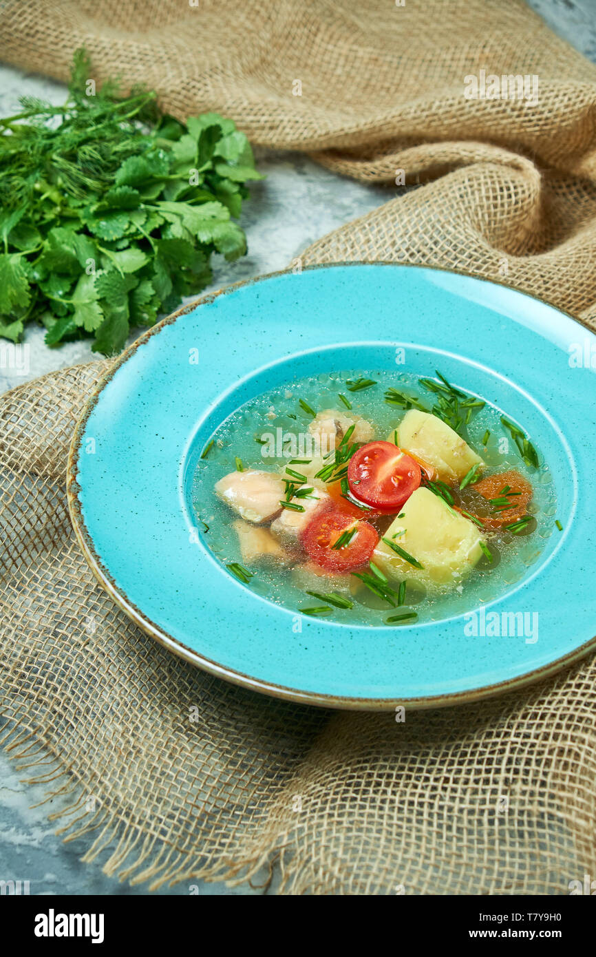 Red fish soup in a blue plate and a bunch of greens on a beige textured ...