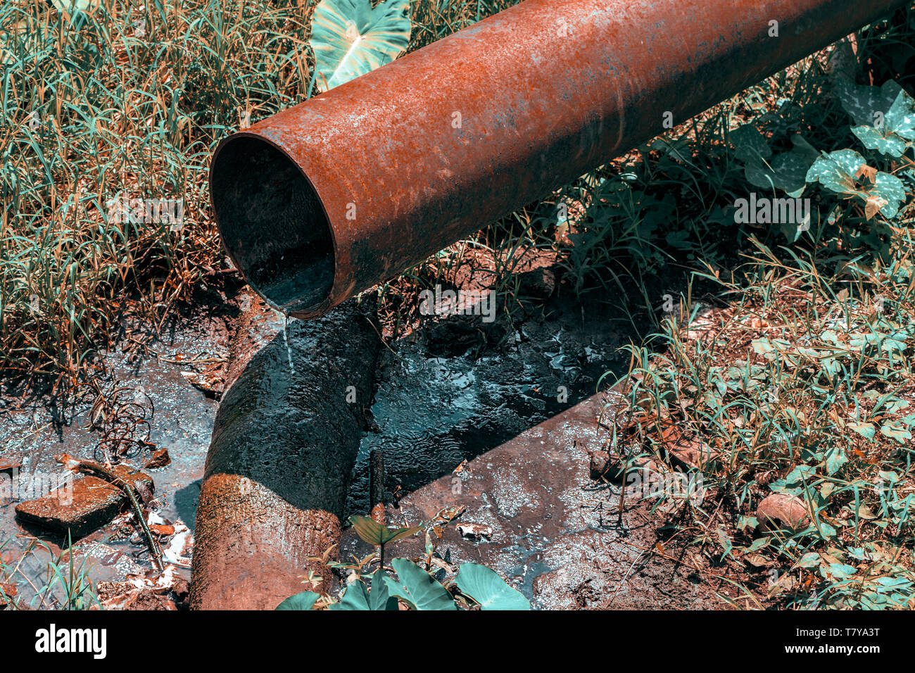 A rusty iron pipe pouring dirty water into a puddle Stock Photo - Alamy