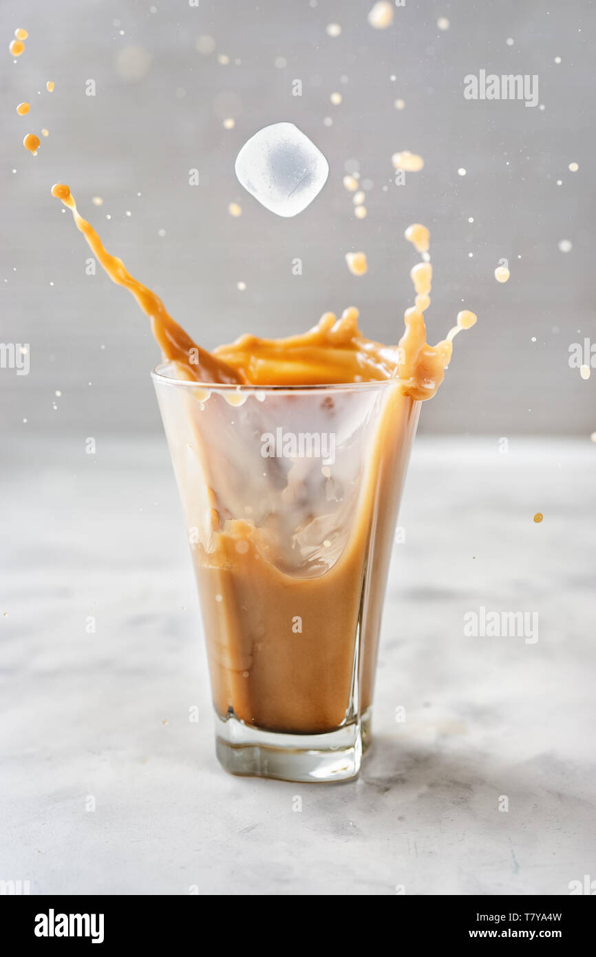 Iced coffee with splash on glass over grey background. Vertical shot ...
