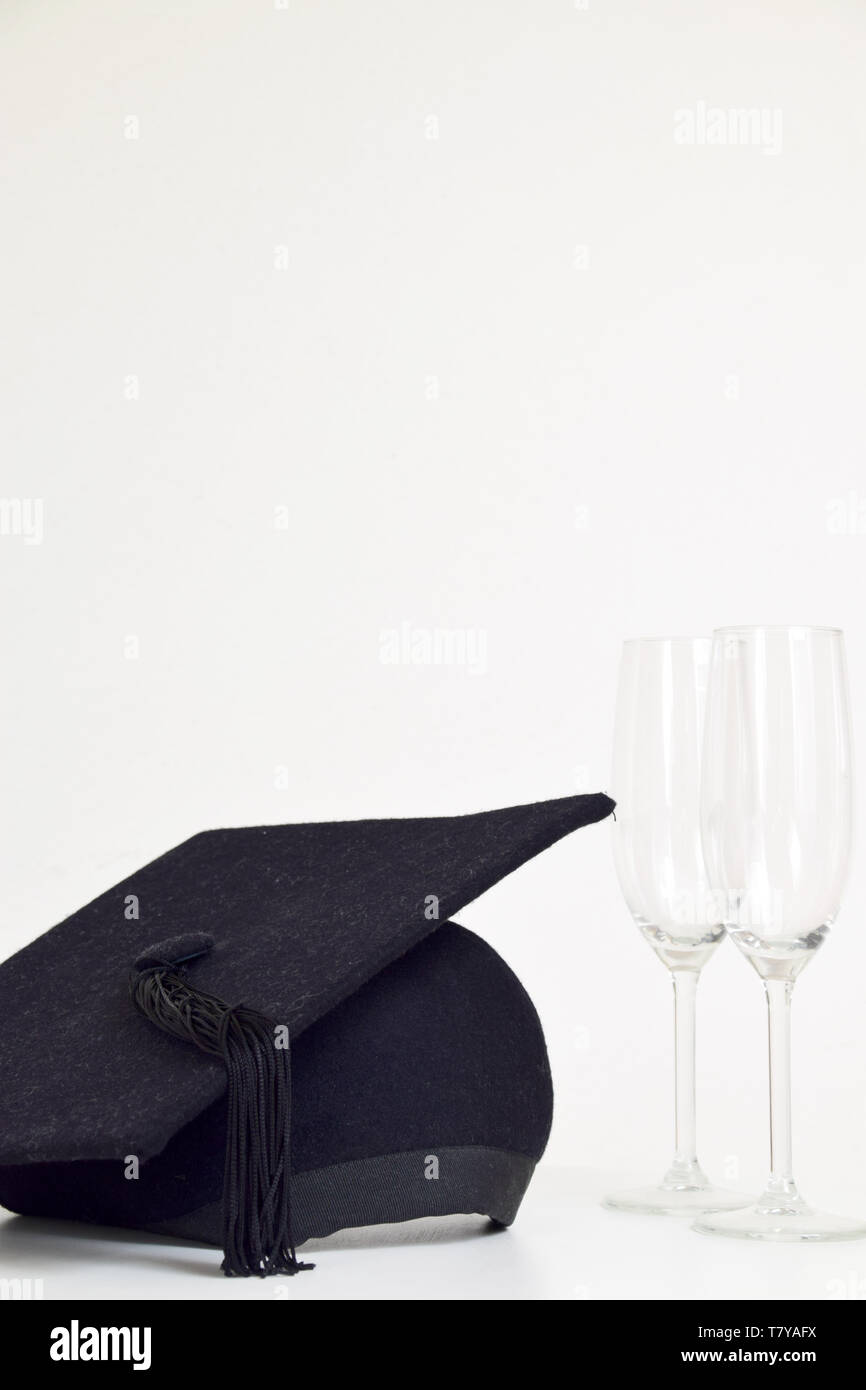 Graduation cap and champagne glasses on table with a white wall in the ...