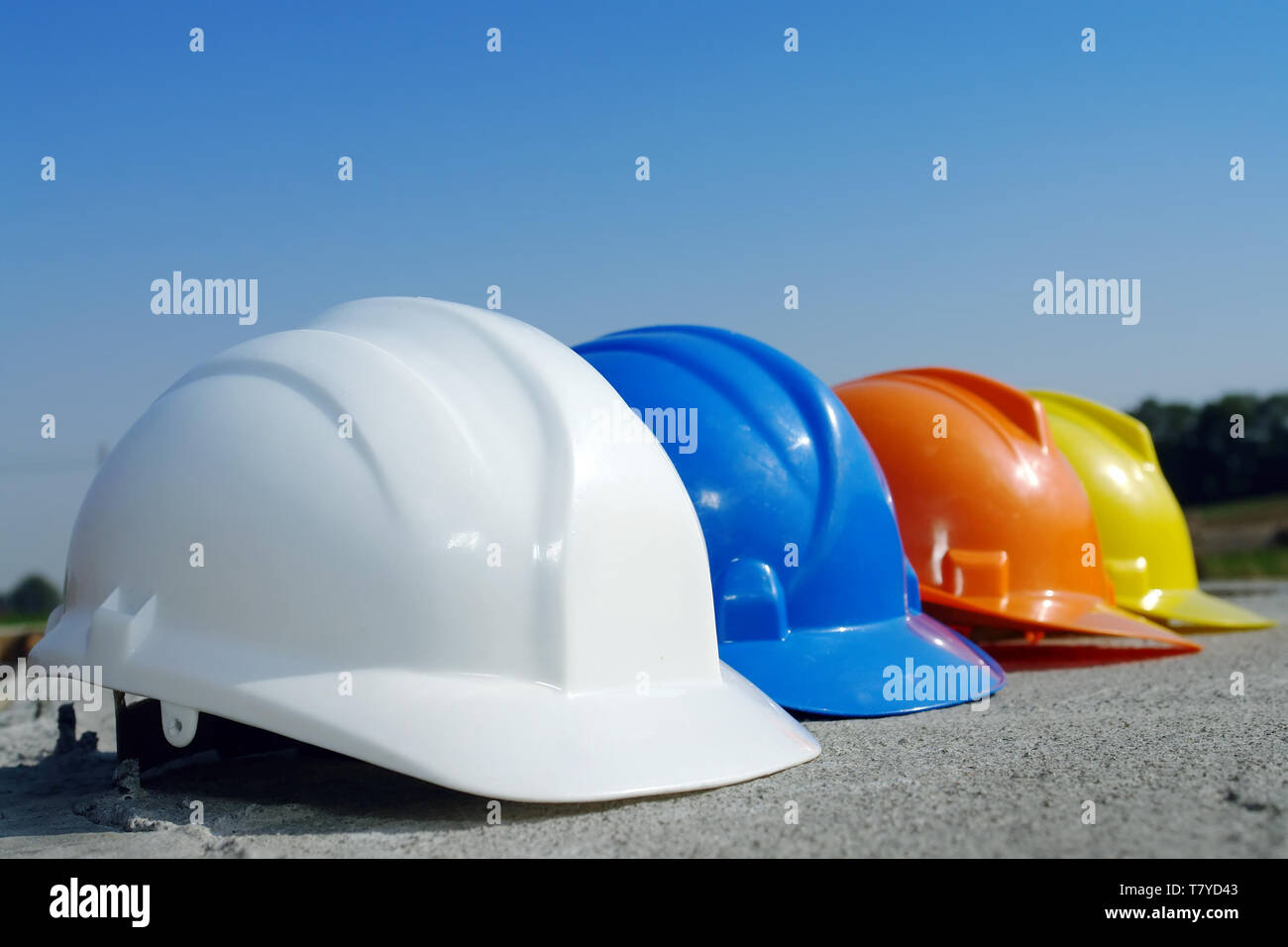 Closeup of row of four hard hats in white, blue, orange and yellow ...