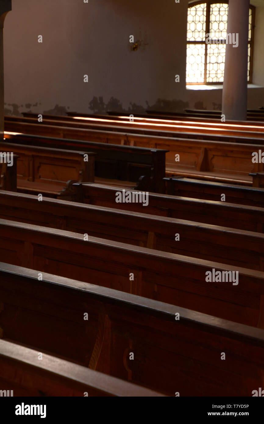 rows of wooden church benches lit by the sun through colored windows ...