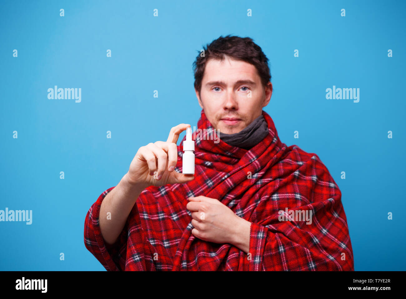 A wrapped in a blanket sick man is standing with nasal spray in his ...