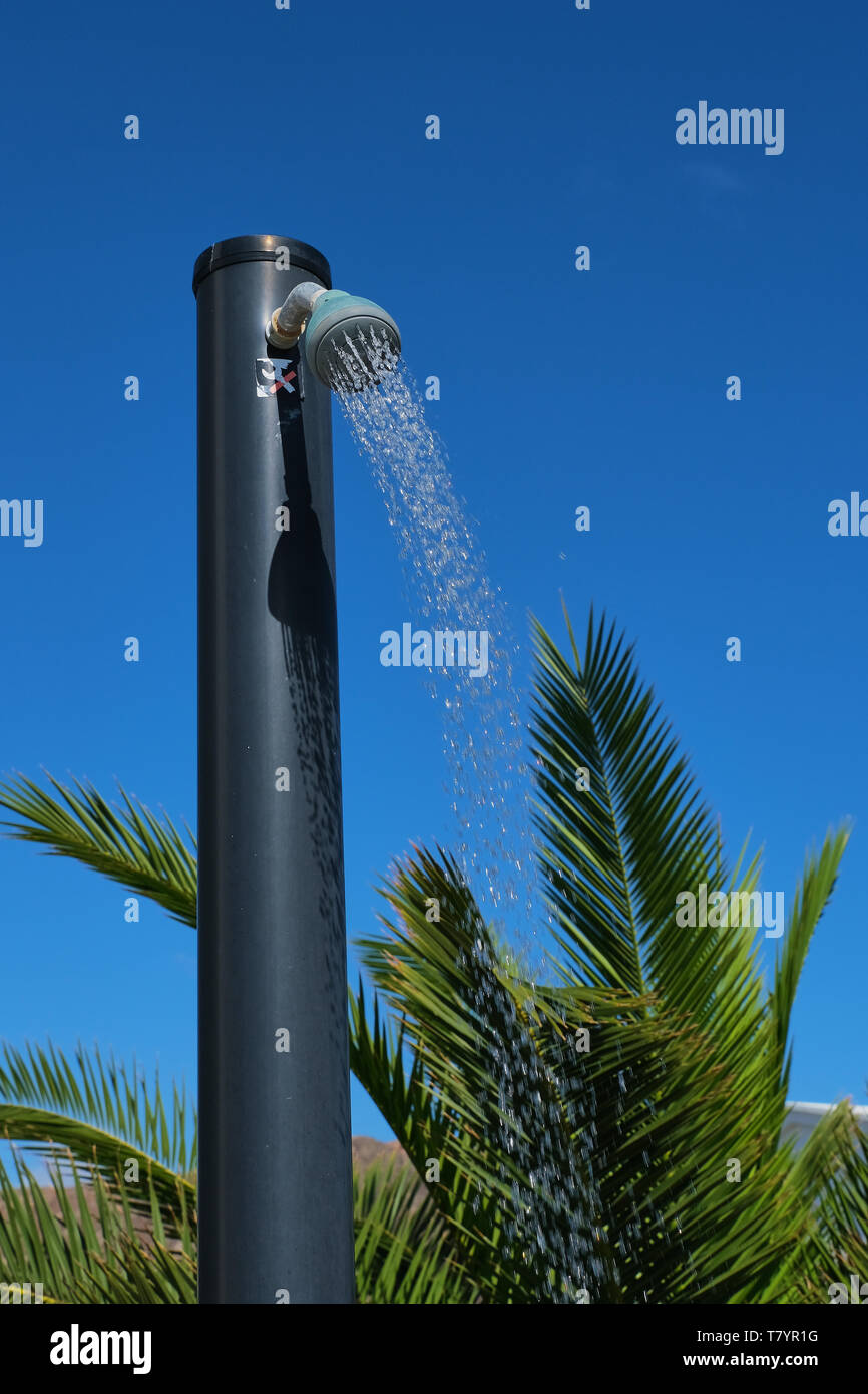 poolside shower with flowing water against blue skyand part of palm ...