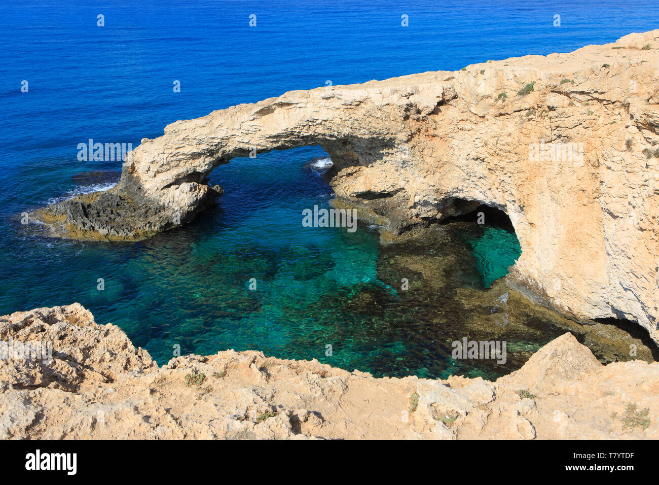 The "Love Bridge", a natural stone arch, amidst shallow turquoise water ...