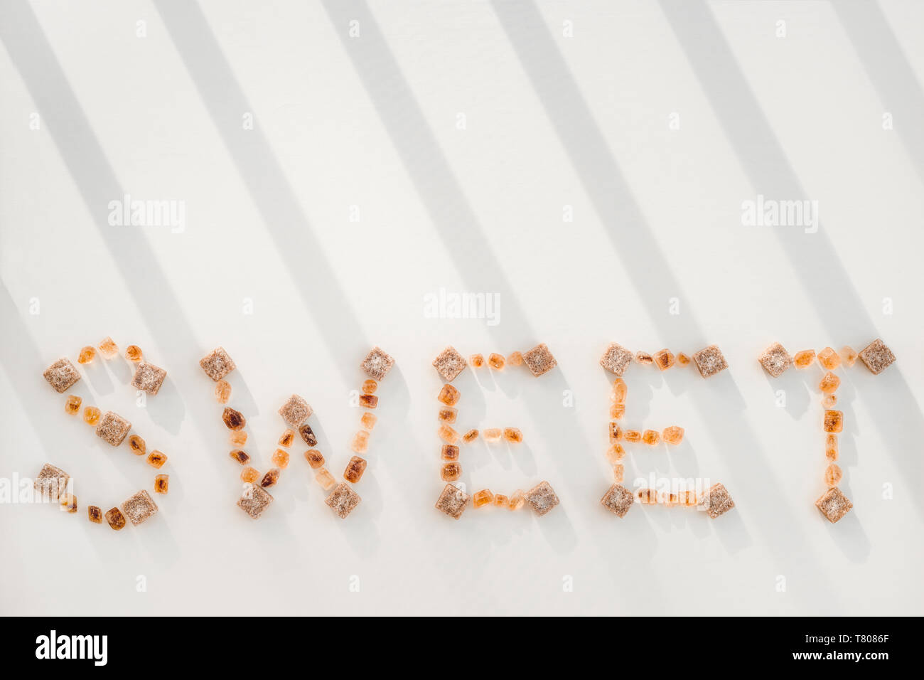 The word SWEET written with brown sugar pieces, in sunlight, on white ...