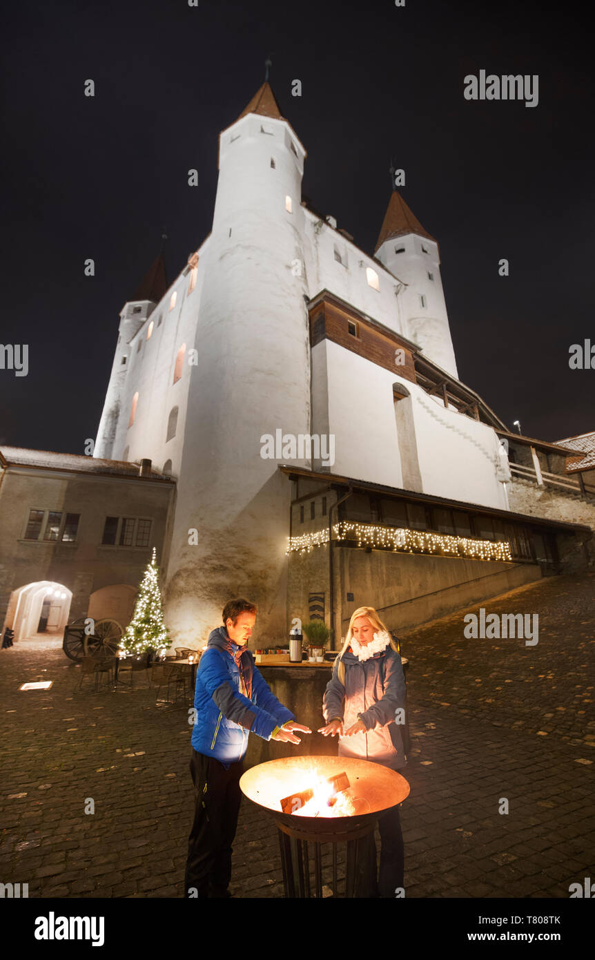 A couple of people warm their hands with the castle in the background ...