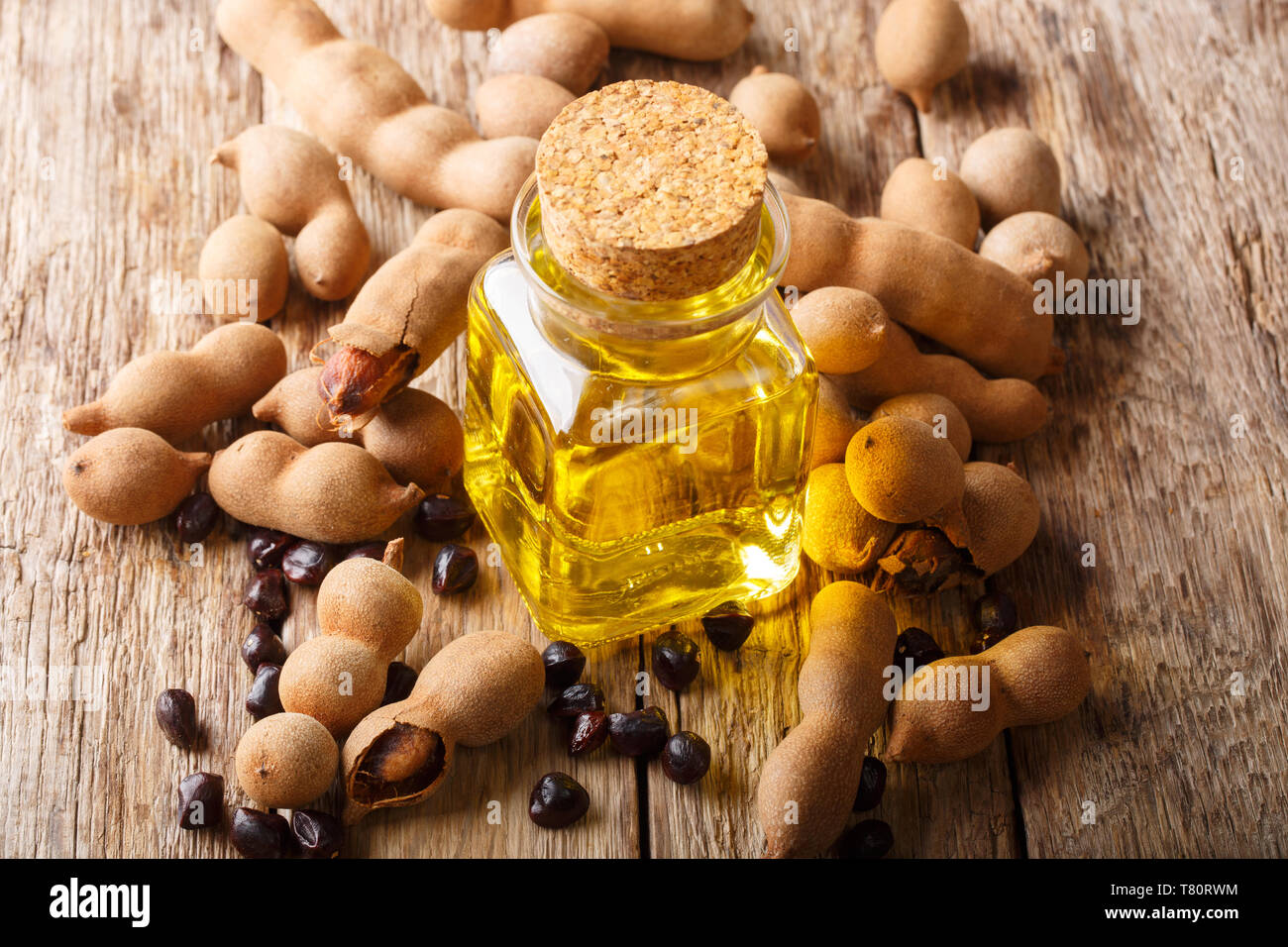 Tamarind seed oil in a glass jar close-up on a wooden table. vertical ...