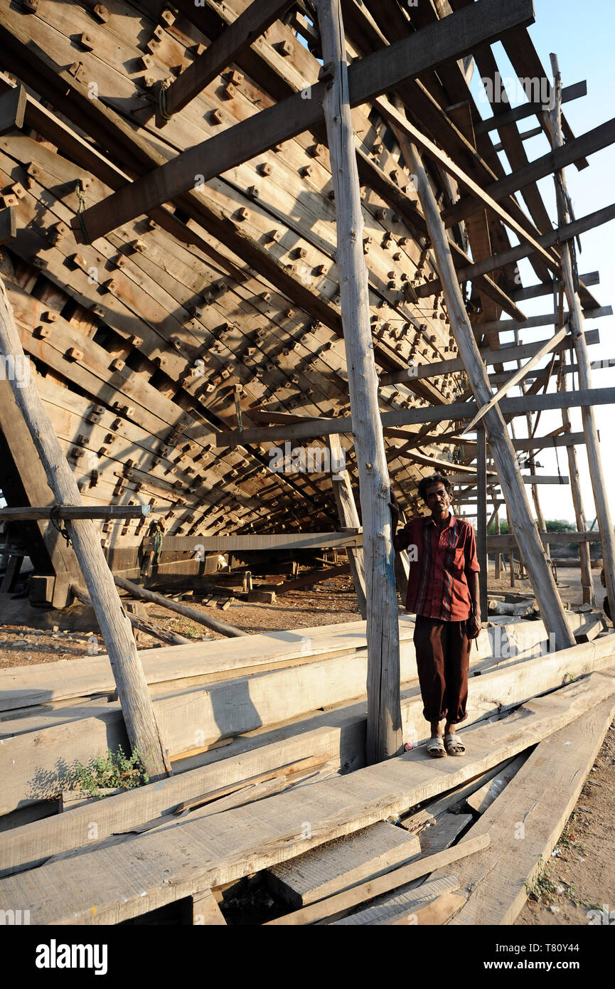 Boatbuilder beneath the hull of ocean going dhow under construction by ...