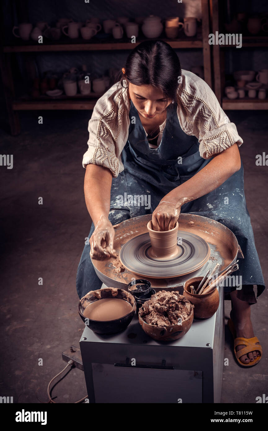 Beautiful young lady making pottery, sculptor from wet clay on wheel ...