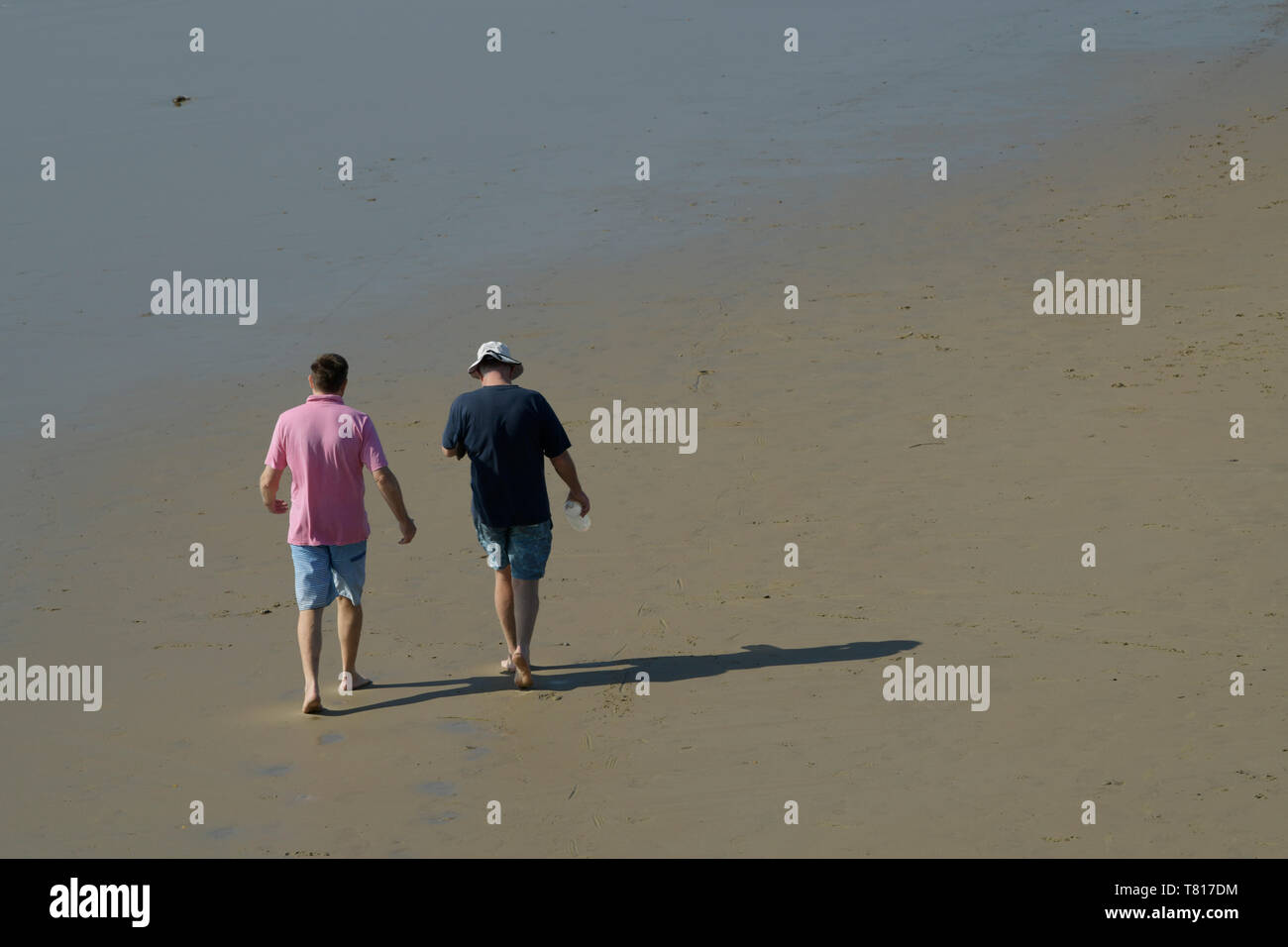 Two adult male companions walking on beach for healthy lifestyle ...