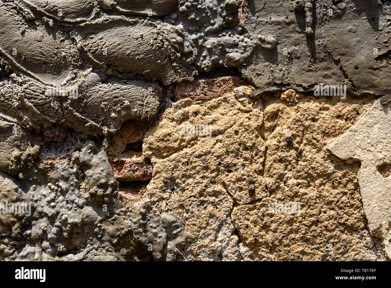 Old weathered masonry wall with crumbling brick and many cement patches ...