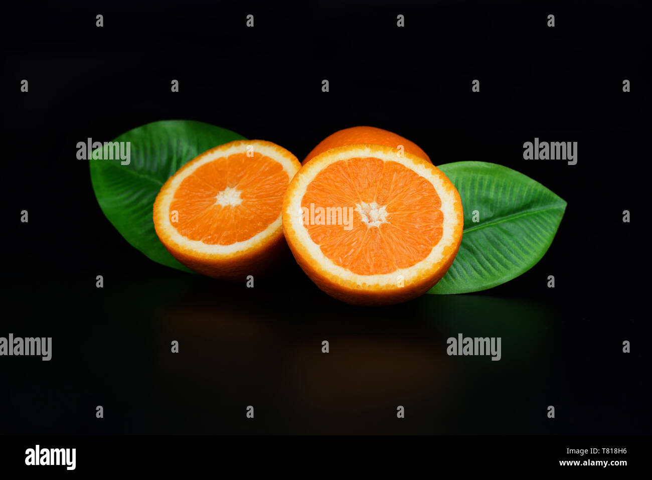 two half ripe orange fruit useful with leaf on an isolated black ...