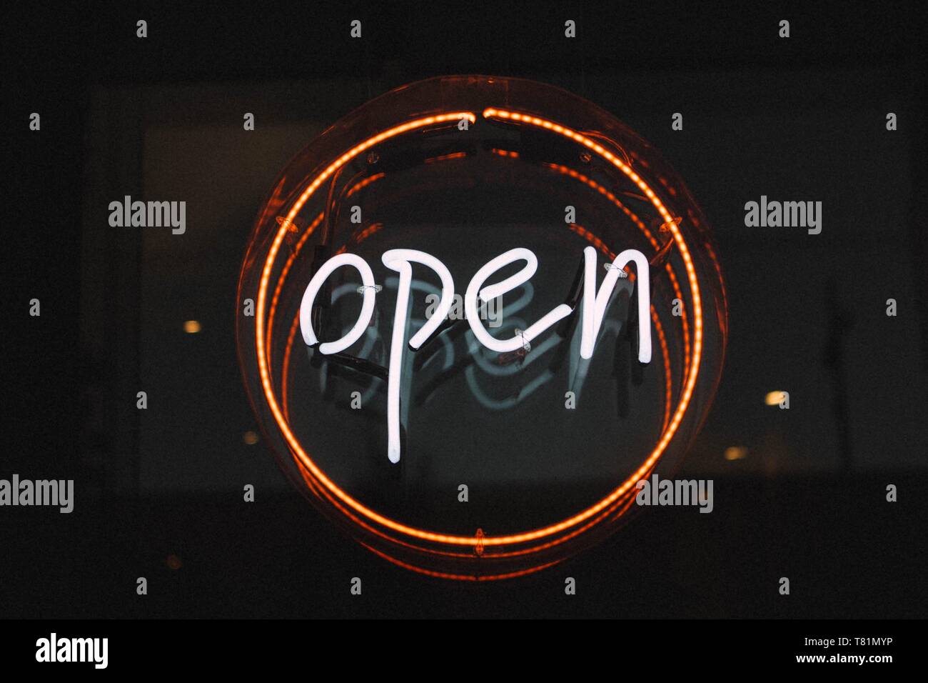 a white neon "open" sign surrounded by an orange ring on a black ...