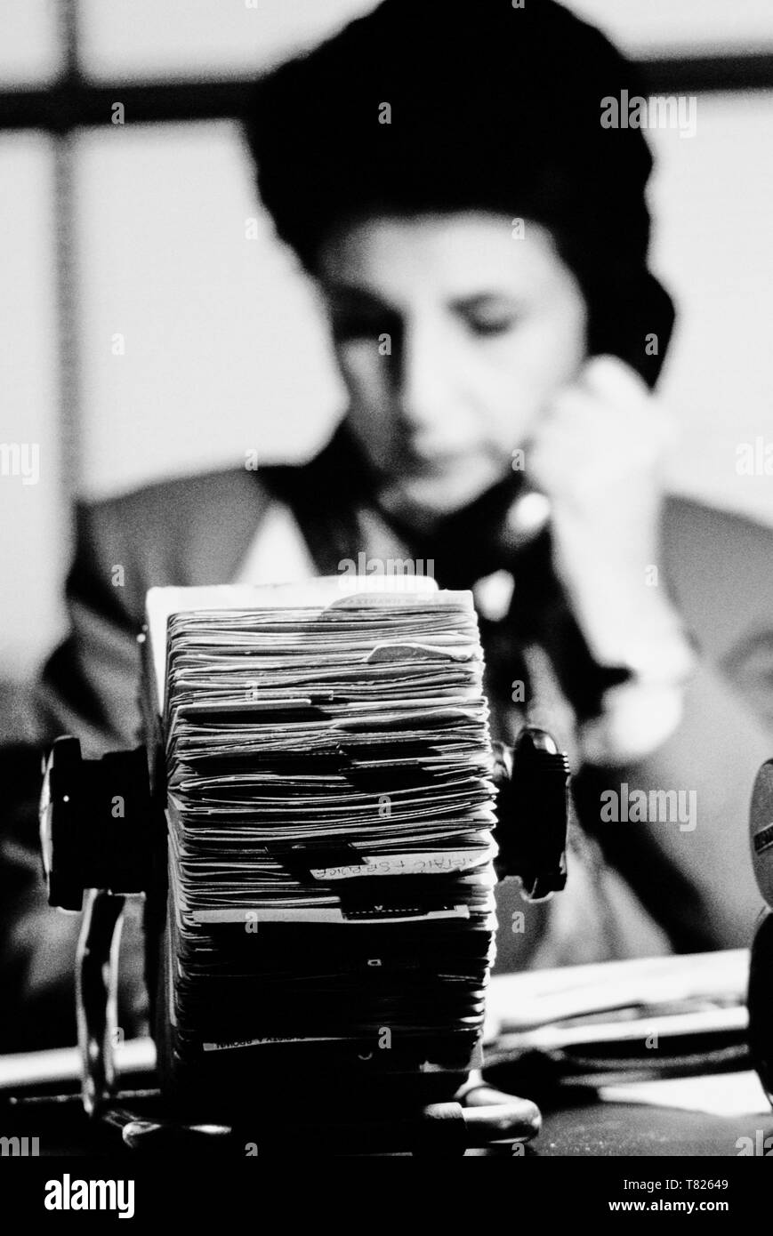 Businesswoman at desk working late with her vintage rolodex card index ...