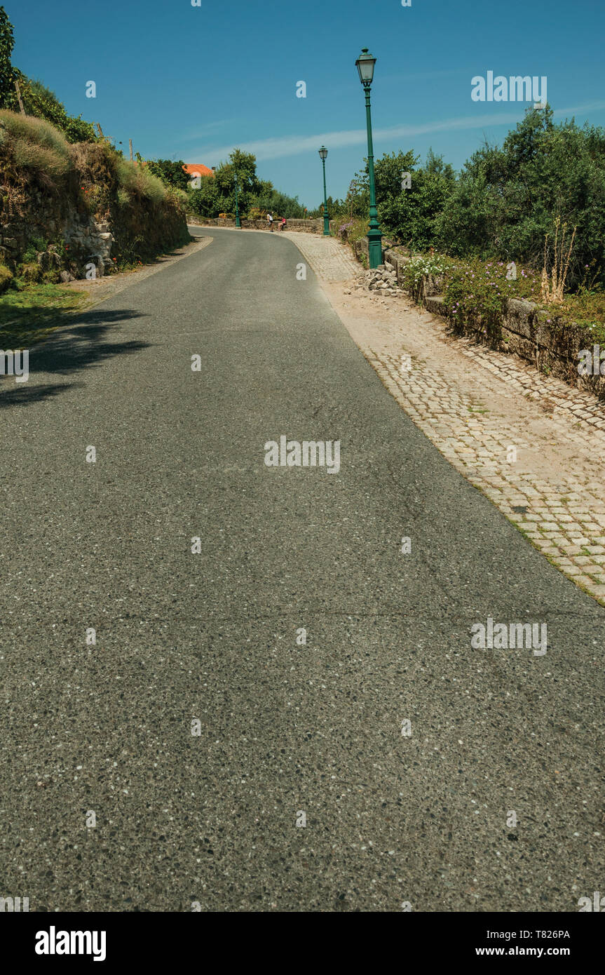 Asphalt road on slope with stone parapet and trees alongside on a sunny ...