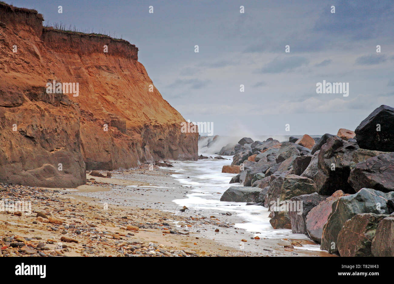 A view of eroding cliffs behind a line of imported rock defences at ...