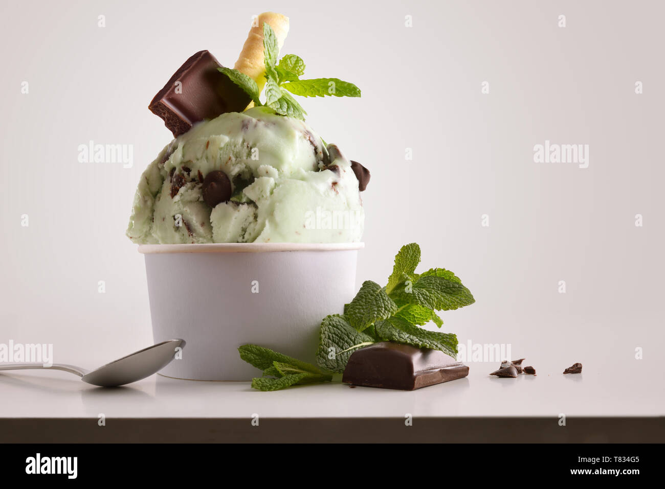 Composition of mint choco ice cream ball in paper cup on white table ...