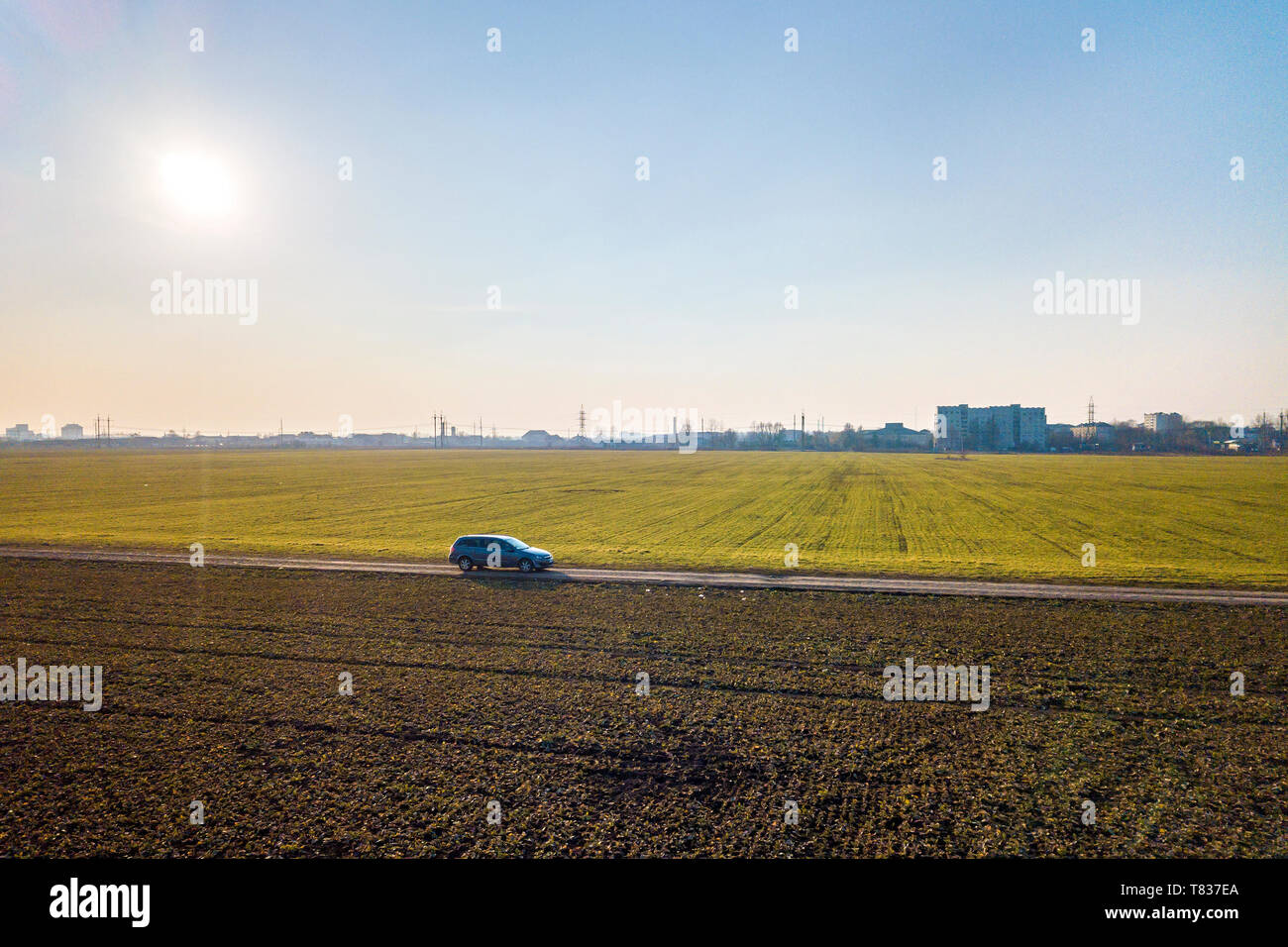 Aerial view of car driving by straight ground road through green fields ...