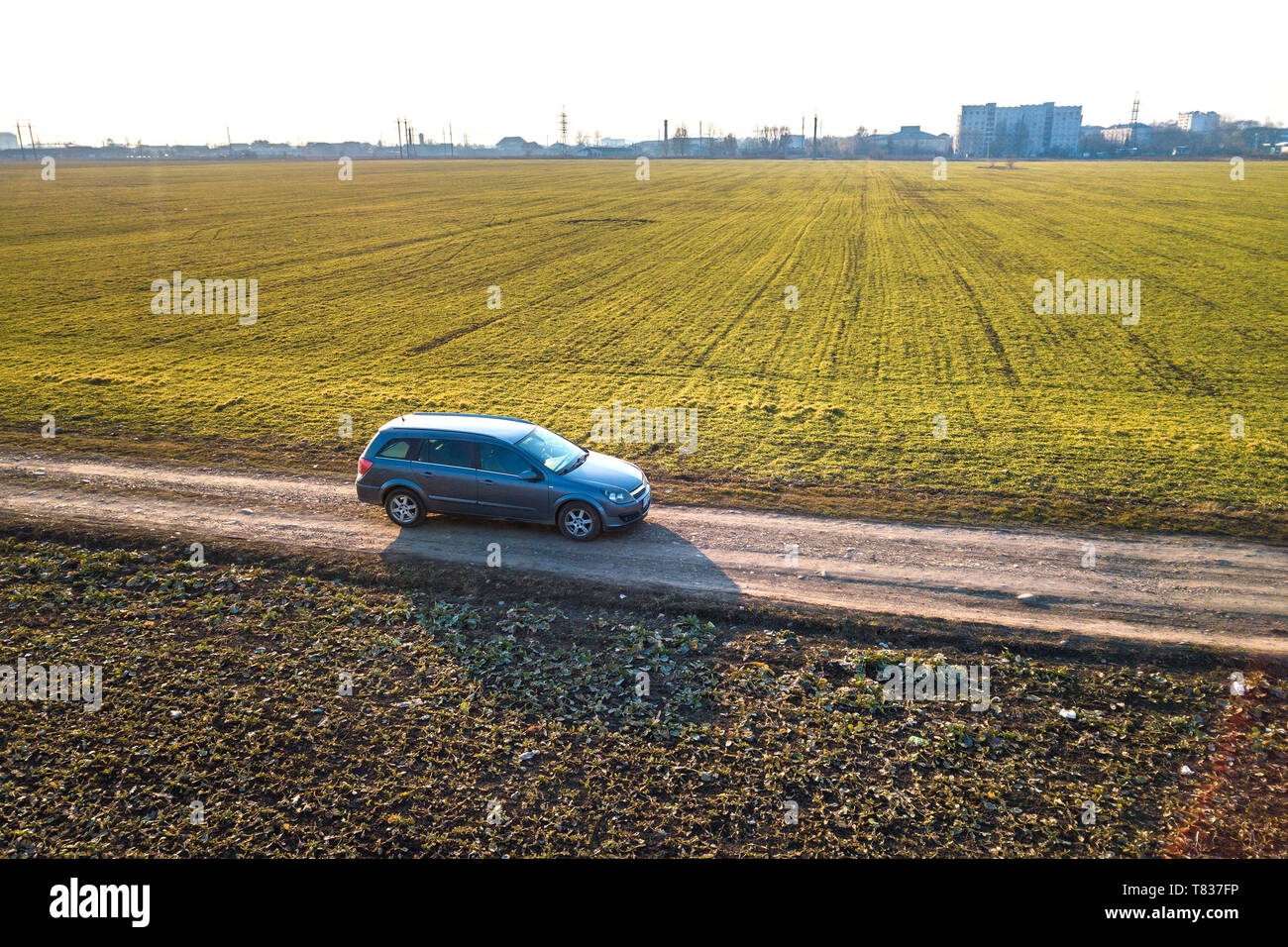 Aerial view of car driving by straight ground road through green fields ...